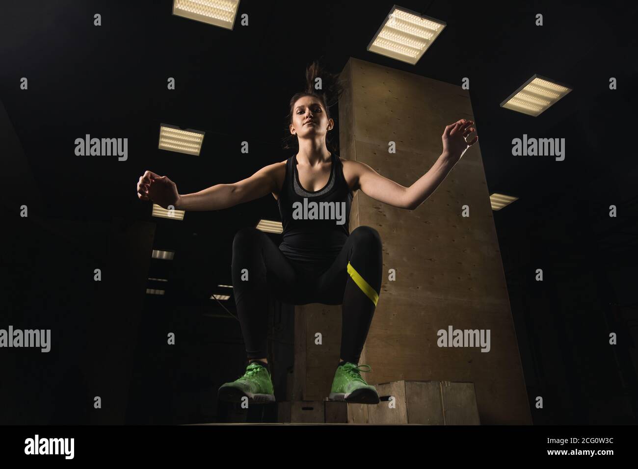 Fit young woman box jumping at a crossfit style gym. Female athlete is ...