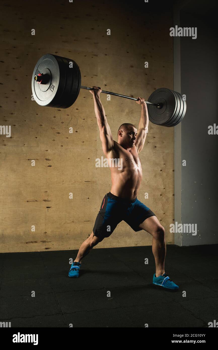 Fit young man lifting barbells looking focused, working out in a gym ...
