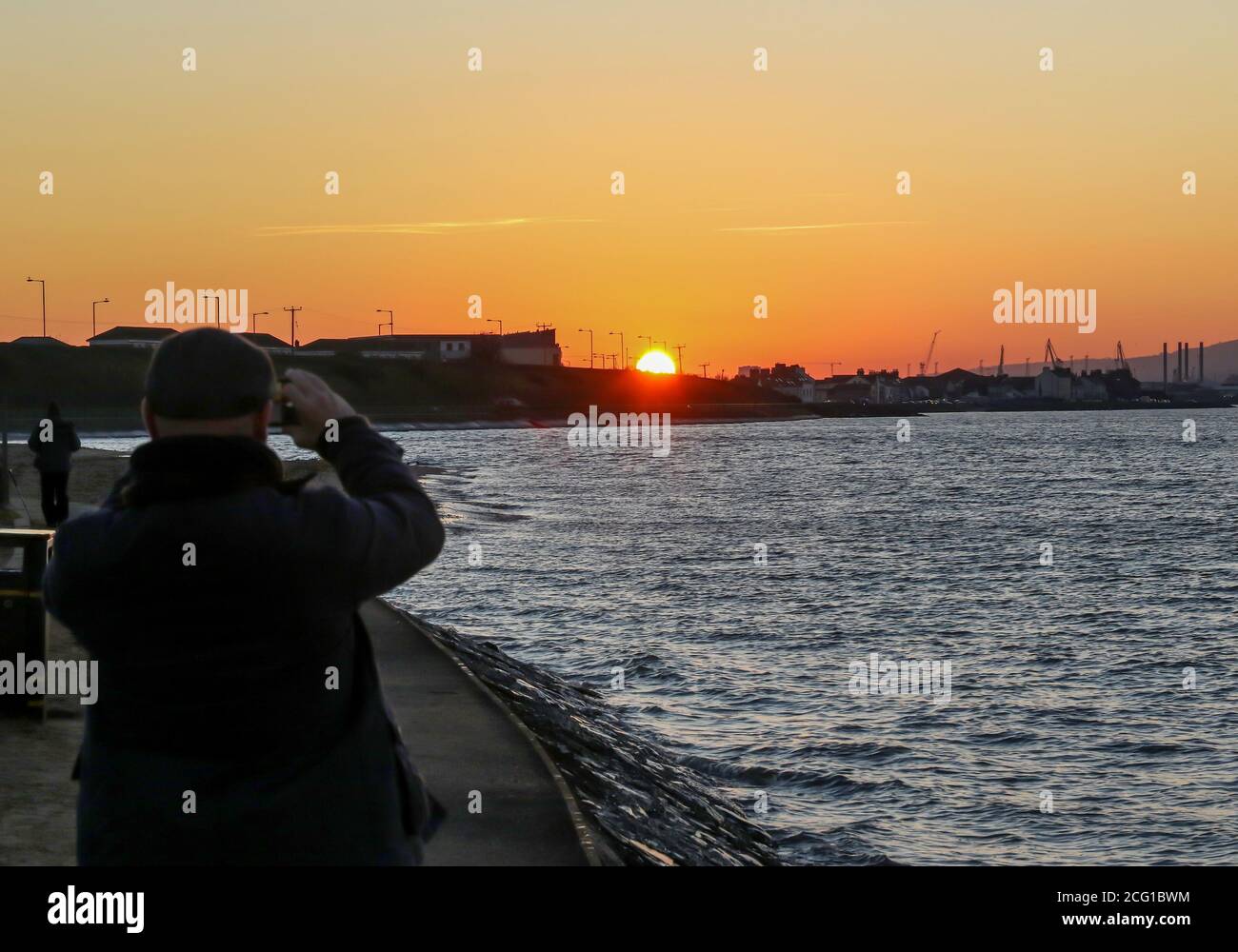Man taking photograph on mobile phone of winter sunset over city of ...