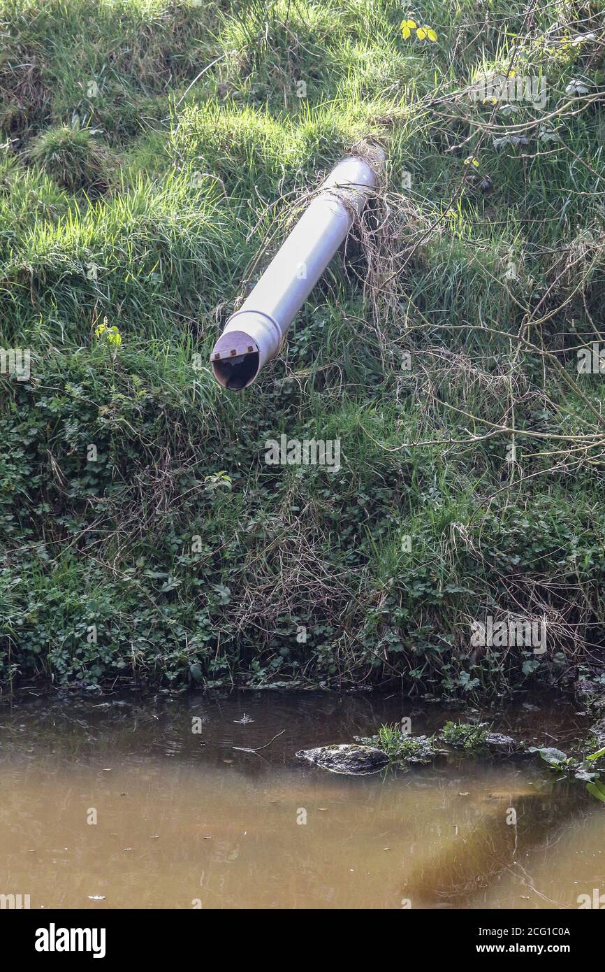 A length of grey upvc plastic pipe sticking out of canal bank with ...