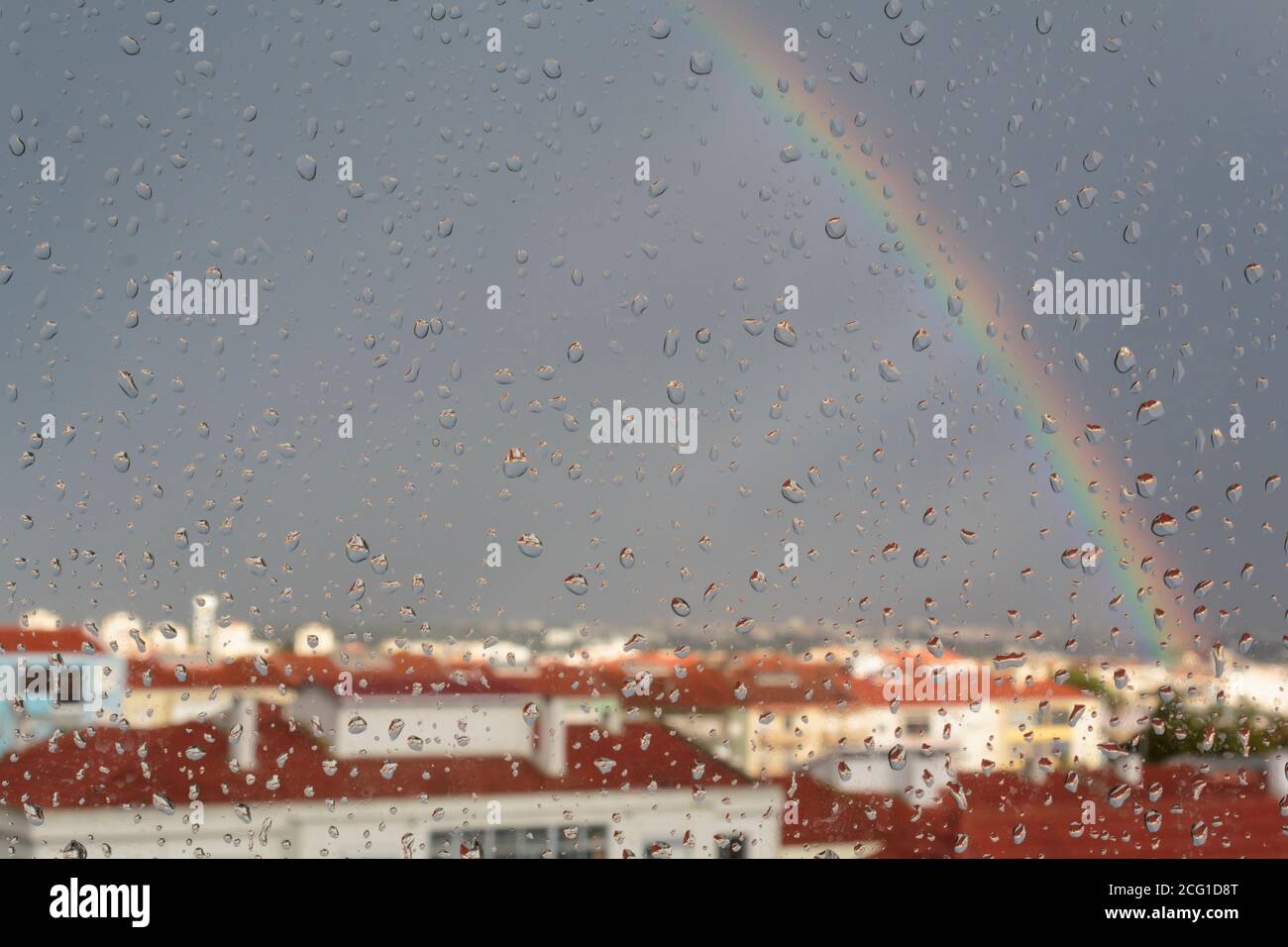 Window with raindrops with rainbow over buildings on the background ...