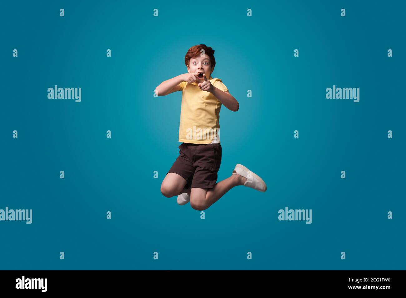 Ginger caucasian boy jumping on a blue studio wall gesturing and ...