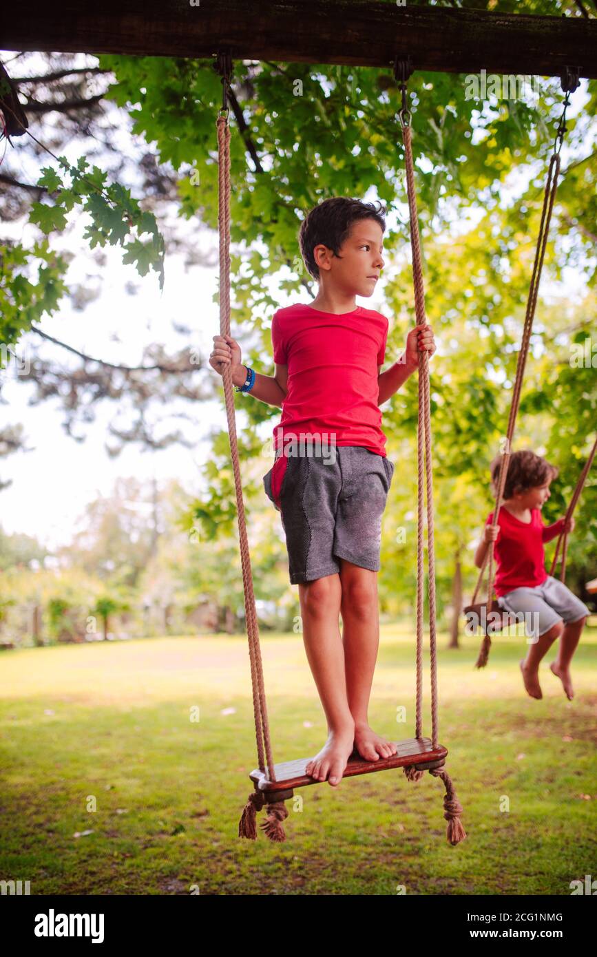 A cute caucasian boy in a red T-shirt is swinging on a swing in the ...