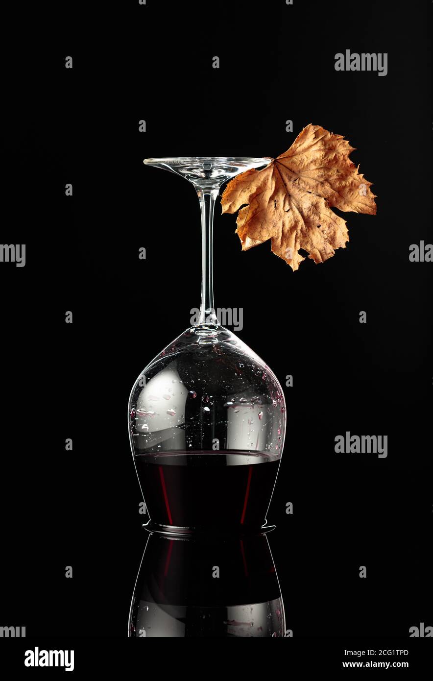 Inverted wine glass with red wine on a black reflective background ...