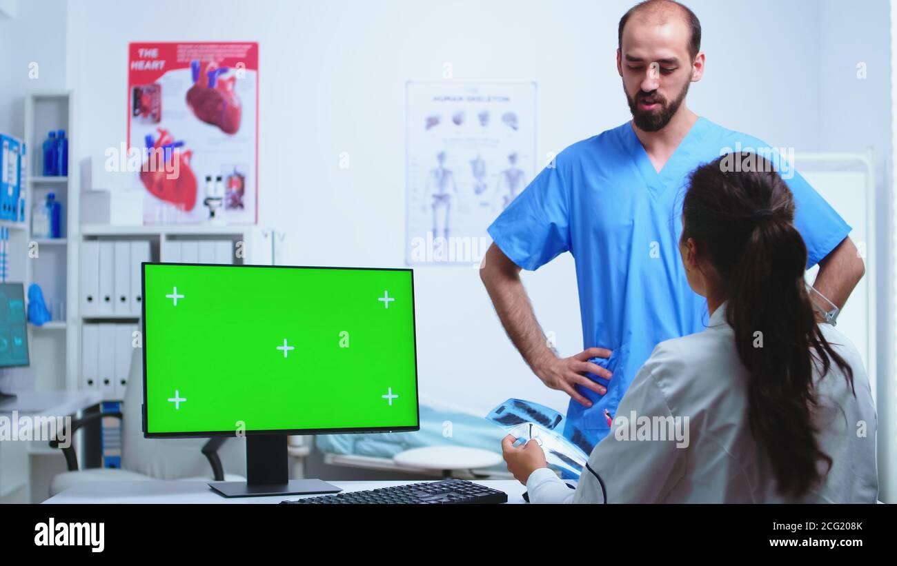 Assistant giving doctor x-ray image while working on computer with ...