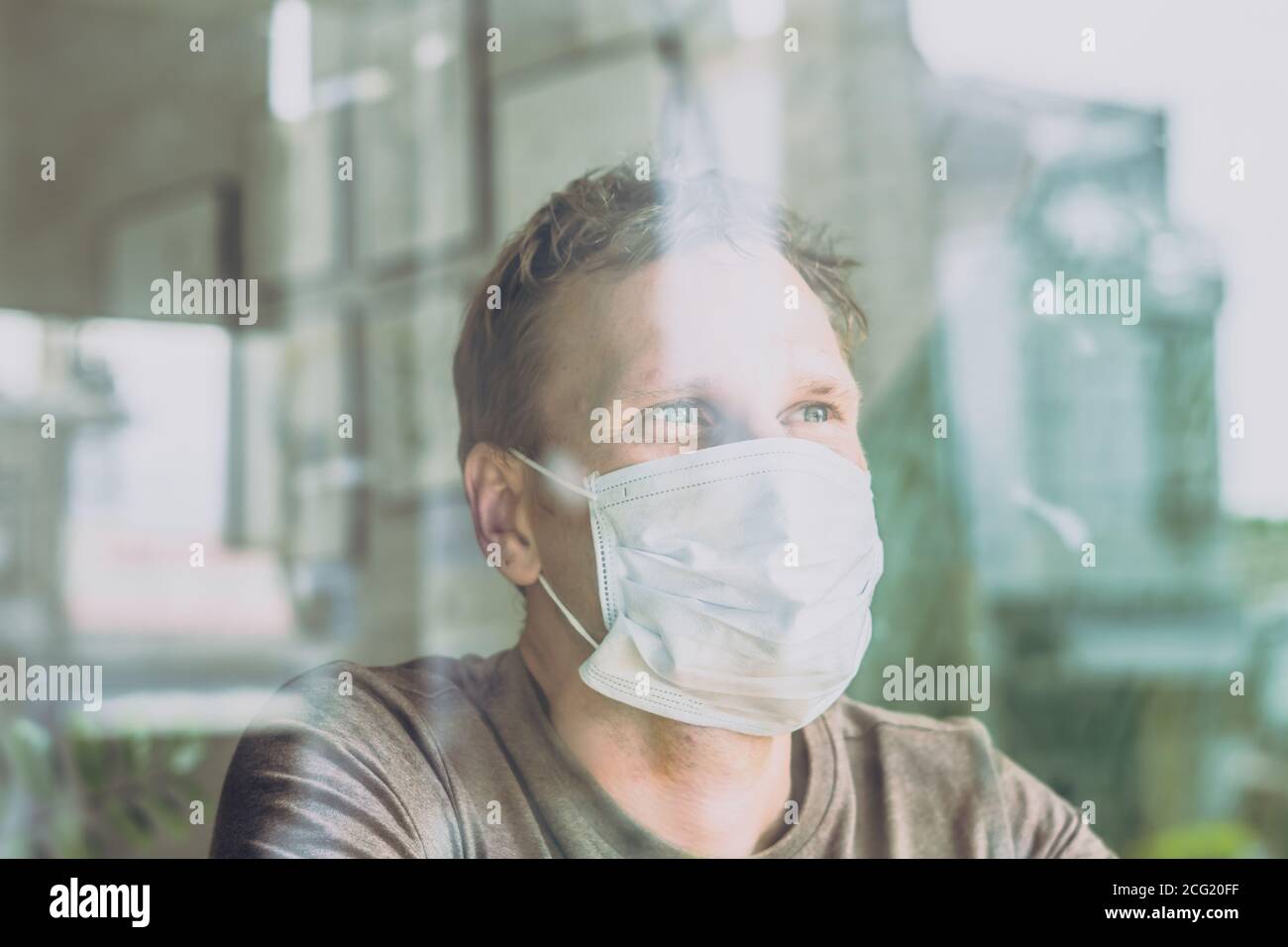 Portrait Man wear white protective mask, looking outside through window ...