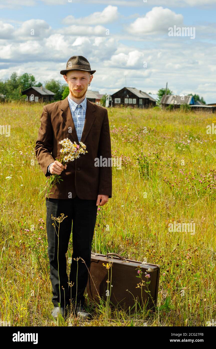 Man hipster with old retro suitcase and wildflowers bouquet in country ...