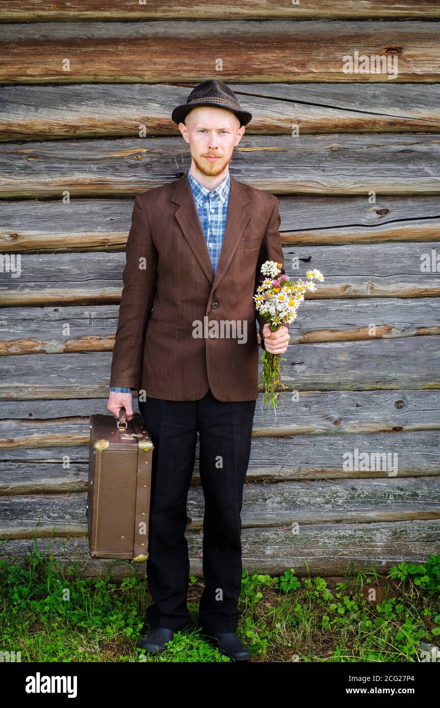 Man hipster with old retro suitcase and wildflowers bouquet in country ...