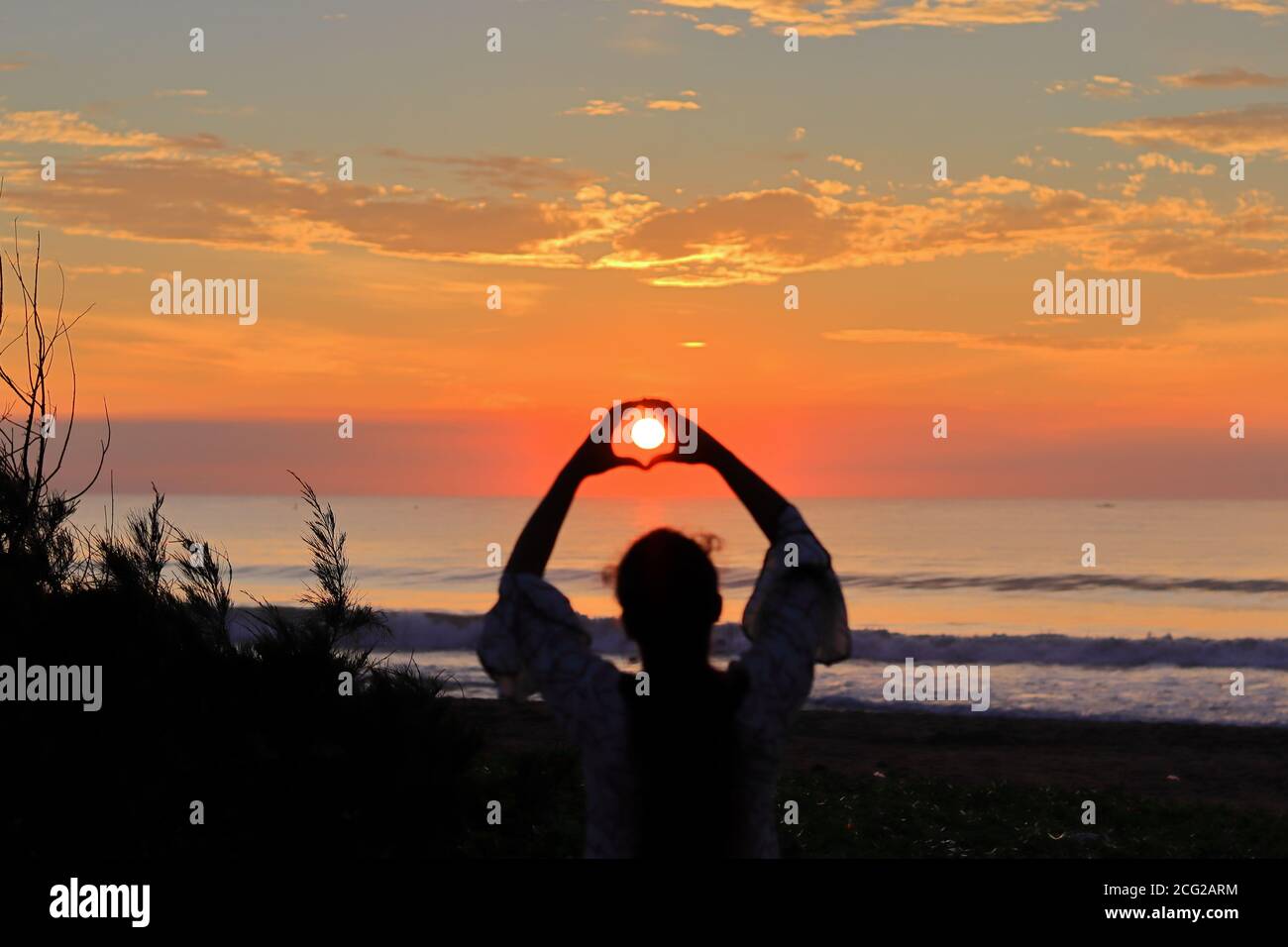 woman hand in heart shape with sunrise in the middle and beach ...
