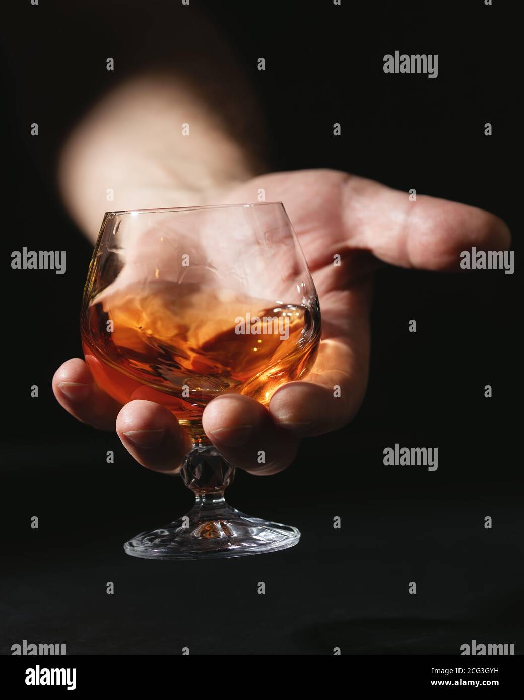 Cognac glass in man's hand. Bright amber drink. Dark background Stock ...