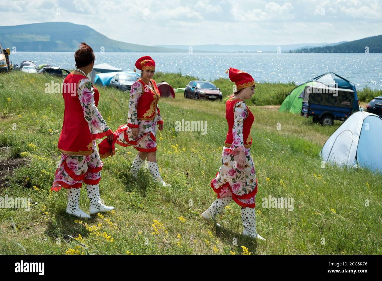 Women in Tatar folk costumes walk along the lake with tents at the ...