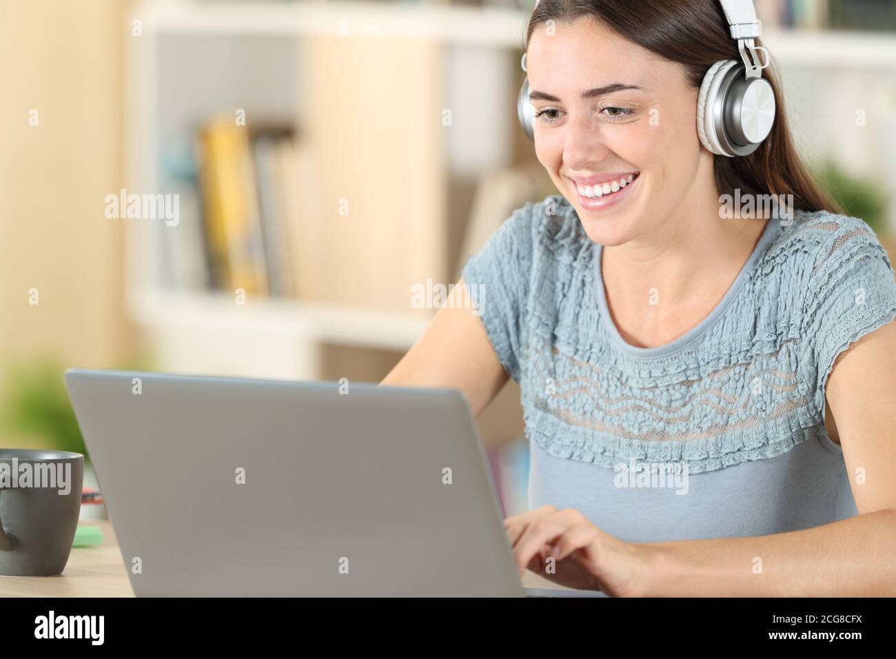 Happy student with headphones and laptop e-learning on a desk at home ...