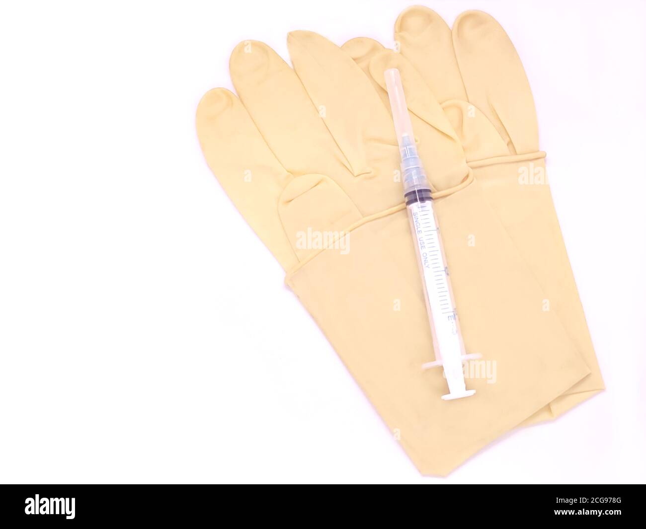 Pair of surgical/ medical gloves and a plastic syringe with cap on ...