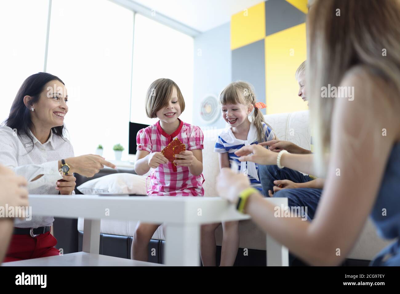 Adults and children are sitting around table holding game cards and ...