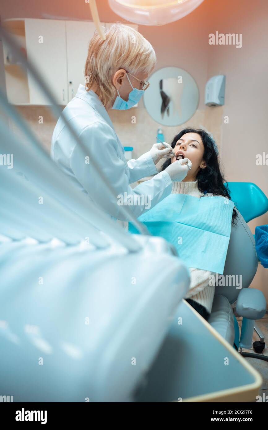 beautiful brunette curly female dentist treat patient in modern clinic ...