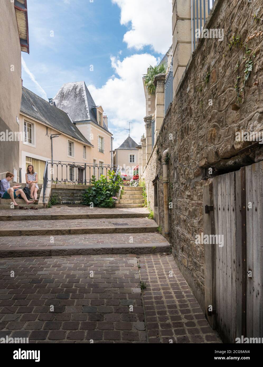 A young couple sitting on steps in the town of Sable sur Sarthe, France ...