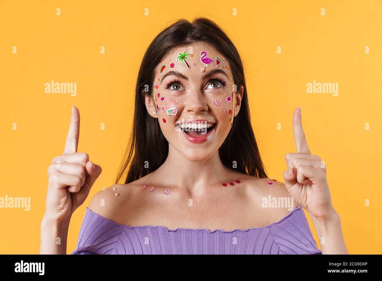 Image of smiling woman with stickers on face pointing fingers upward ...