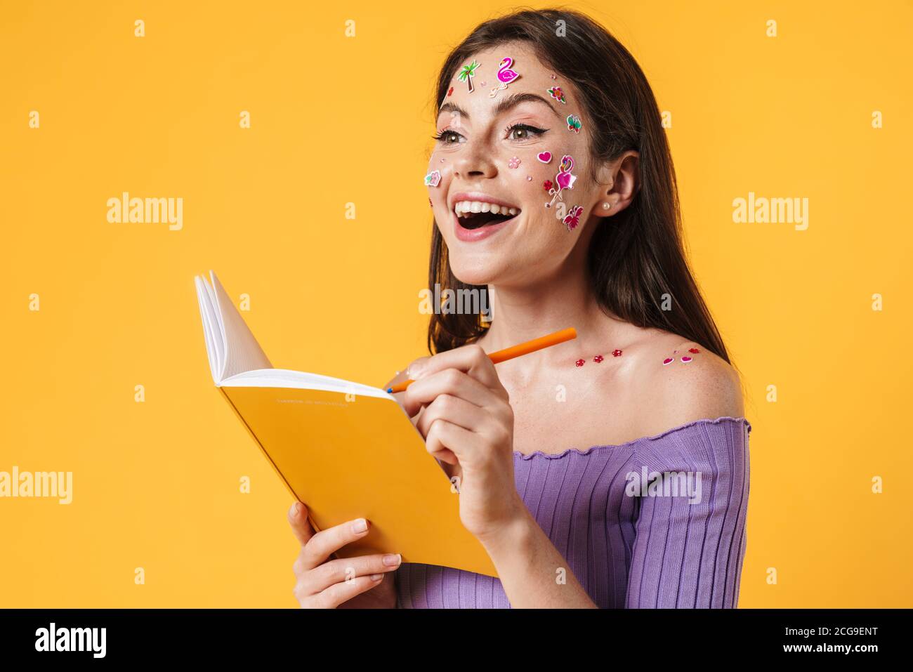 Image of young smiling woman with stickers on face writing in exercise ...
