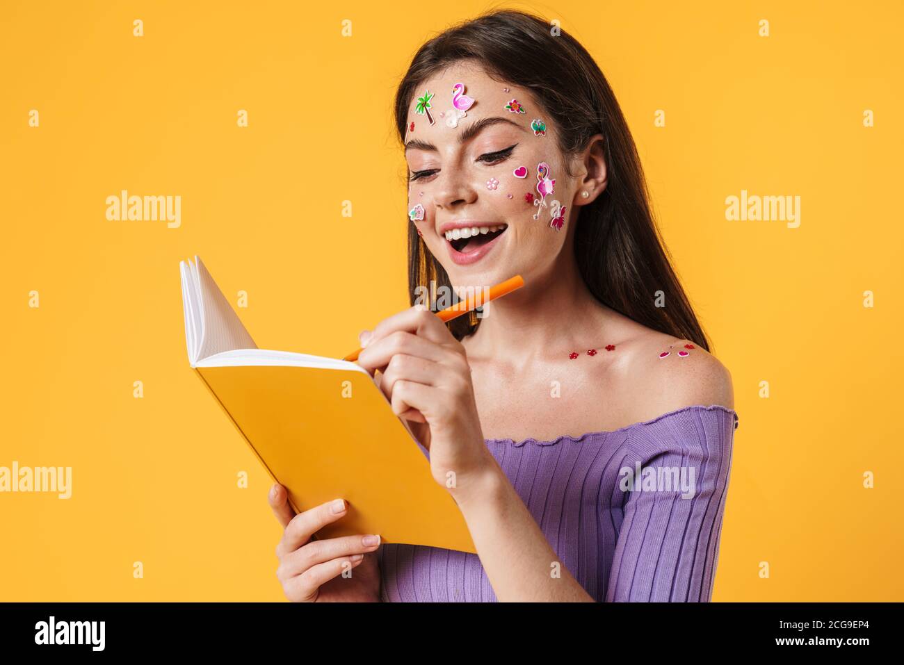 Image of young smiling woman with stickers on face writing in exercise ...