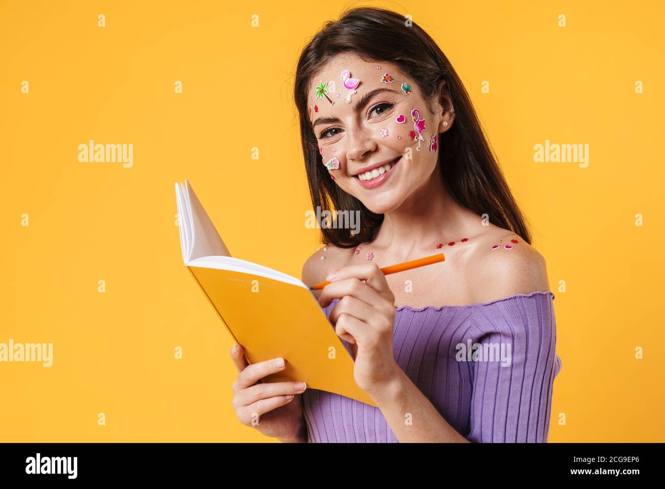 Image of young smiling woman with stickers on face writing in exercise ...