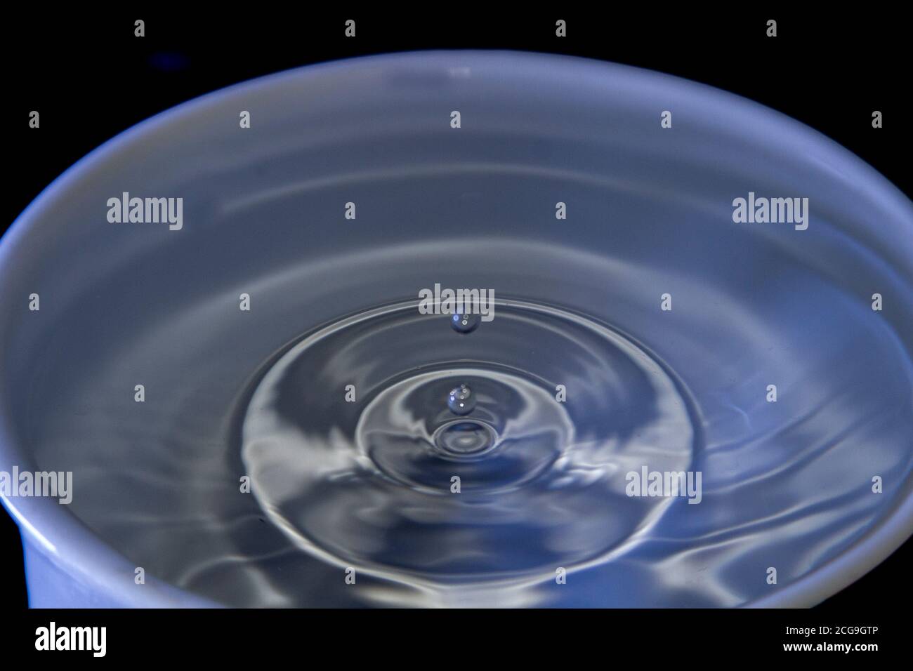 Water drop falling on a cup full with water Stock Photo - Alamy