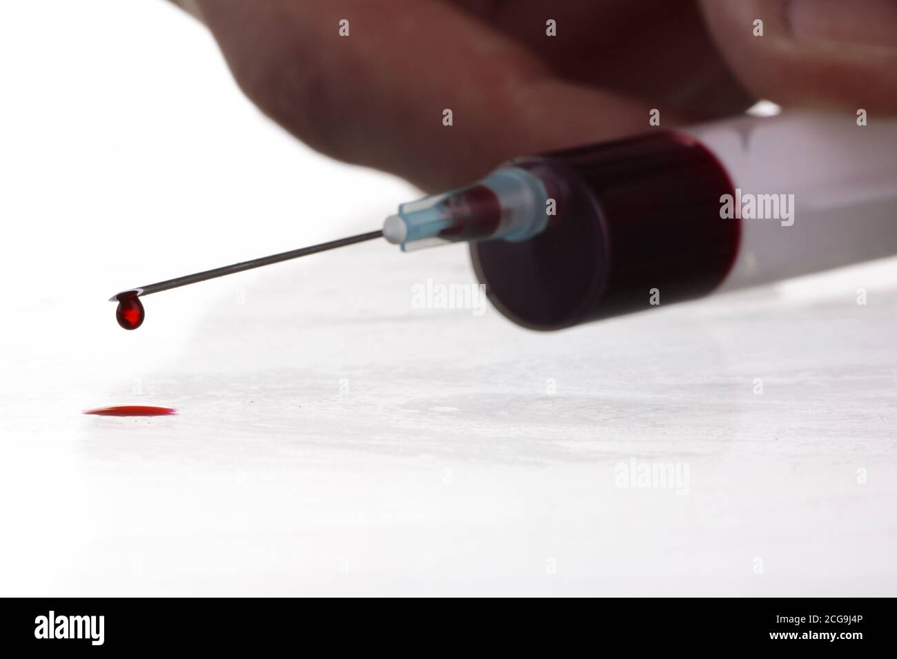 Macro view of drop of blood from syringe with male hand over white ...