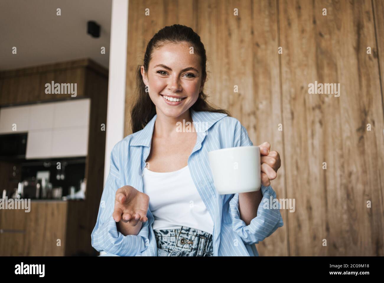 Image of a young positive happy girl indoors at home holding cup of ...