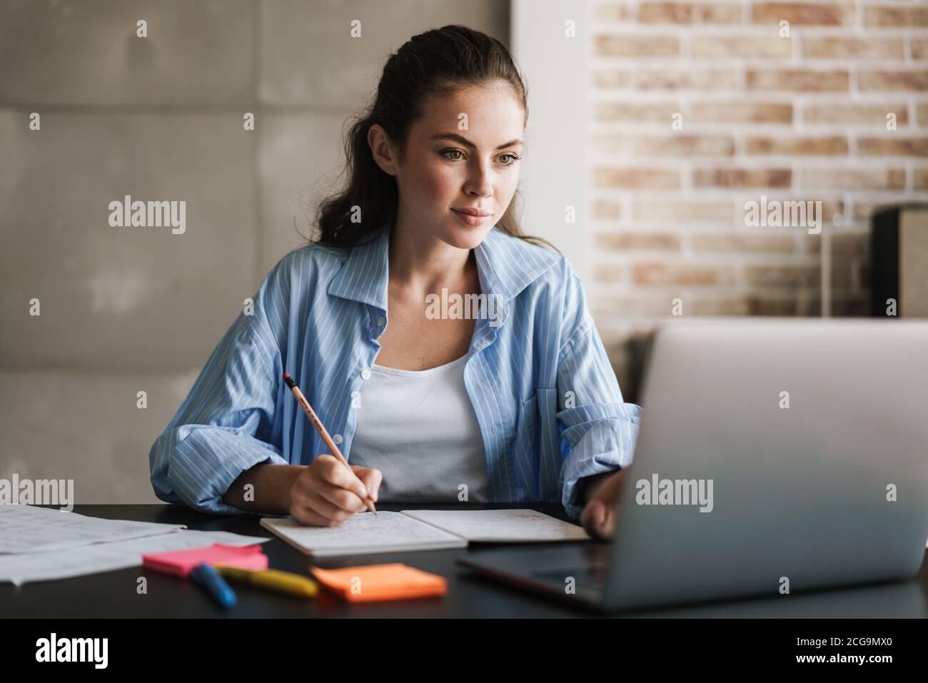 Photo of focused nice girl writing down notes using laptop while ...