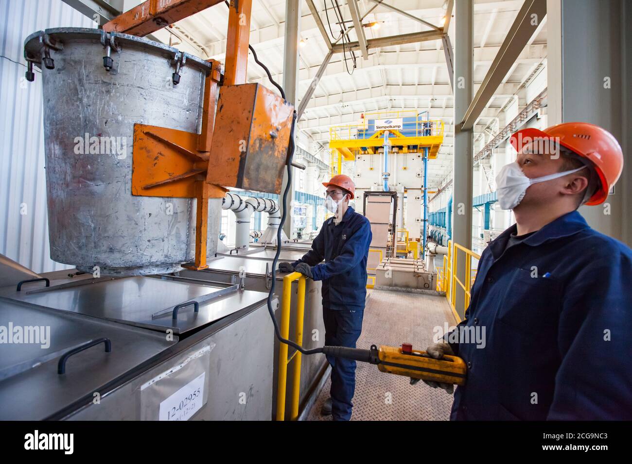 Two workers lifting up metallurgical bucket with metal titanium sponge ...