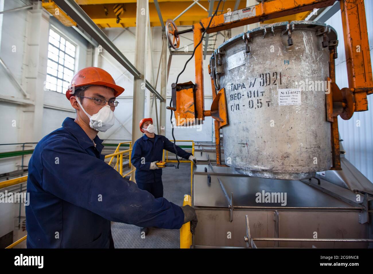 Two workers lifting up metallurgical bucket with metal titanium sponge ...