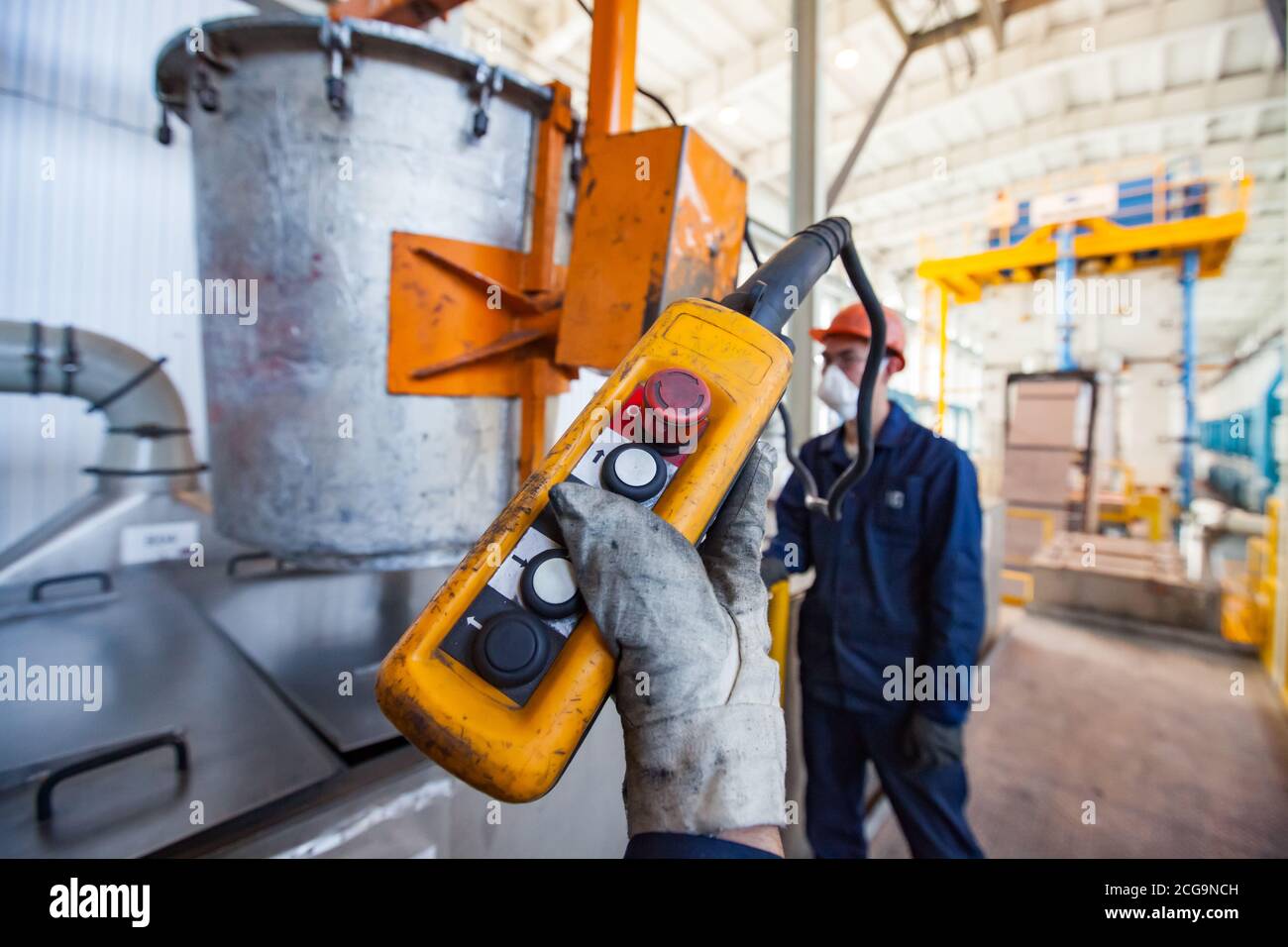 Two workers lifting up metallurgical bucket with metal titanium sponge ...