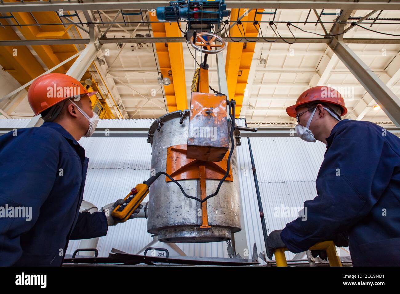 Two workers lifting up metallurgical bucket with metal titanium sponge ...