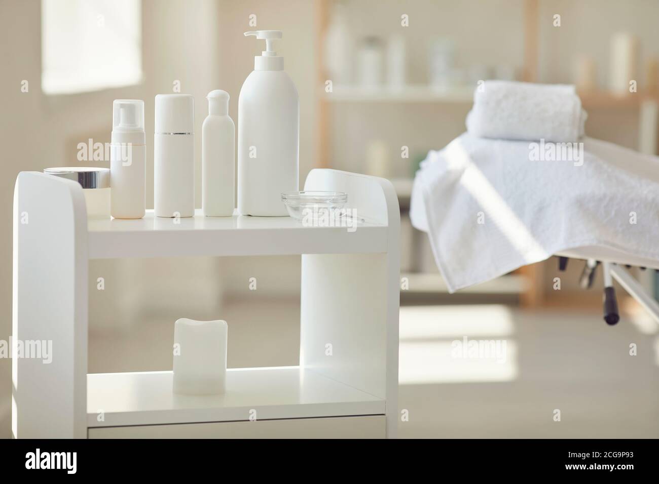 Set of beauty products on small table in spa room with empty massage ...