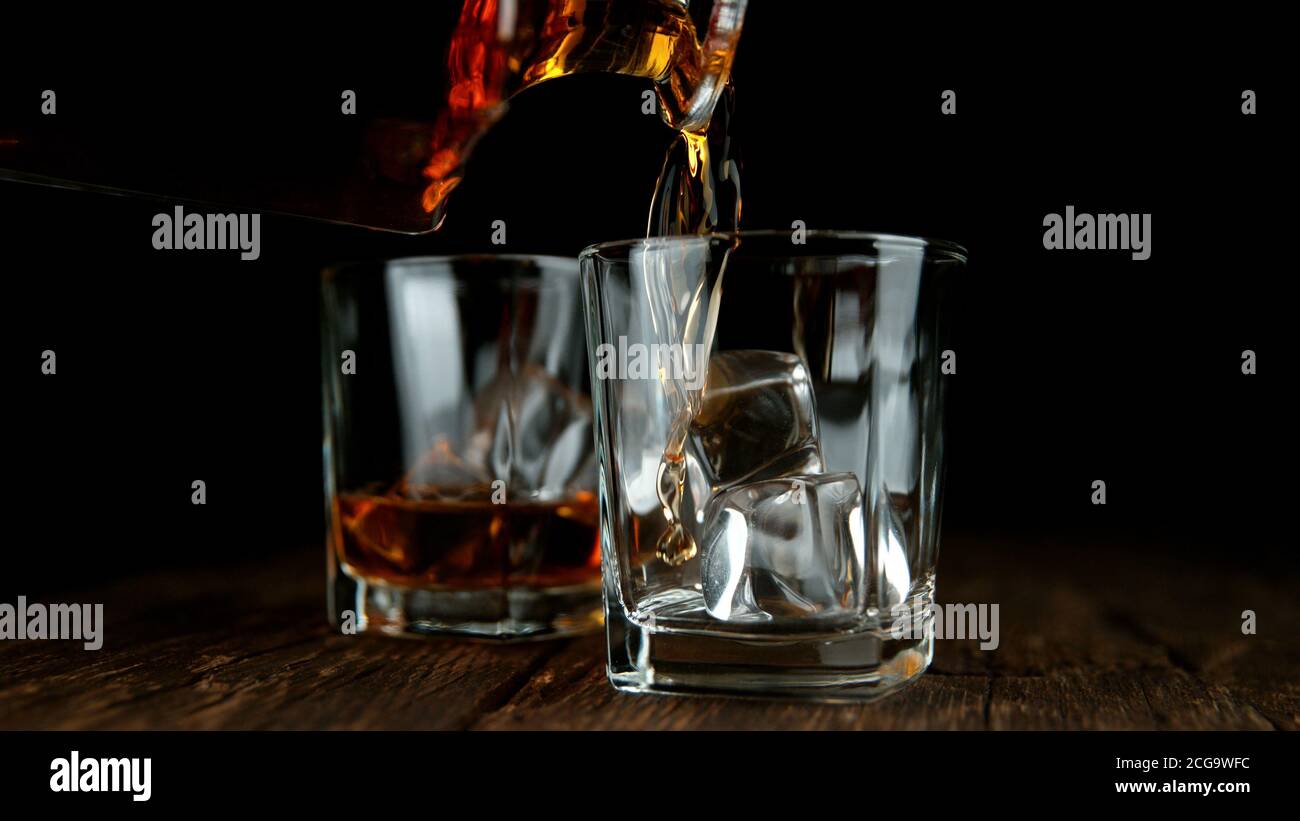 Detail of pouring whiskey into glass on black background Stock Photo - Alamy