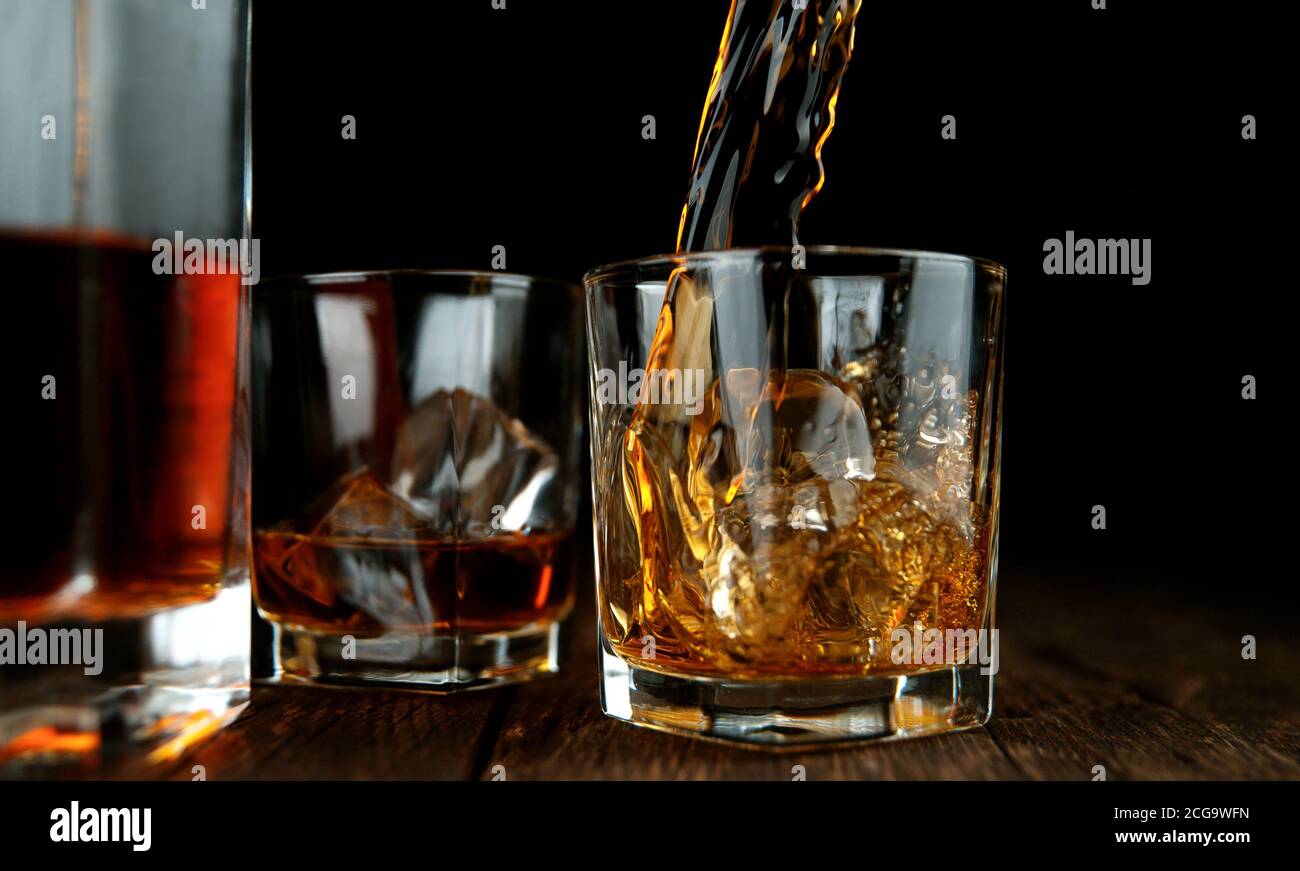 Detail of pouring whiskey into glass on black background Stock Photo - Alamy