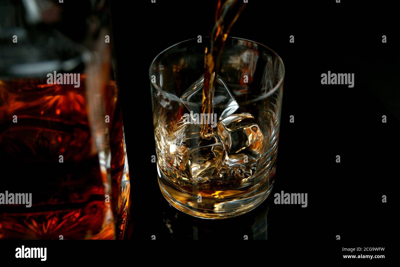 Detail of pouring whiskey into glass on black background Stock Photo - Alamy