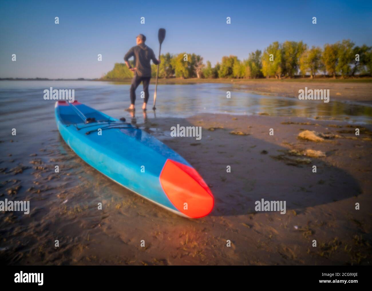 stand up paddler and his paddleboard on a lake beach, soft focus ...