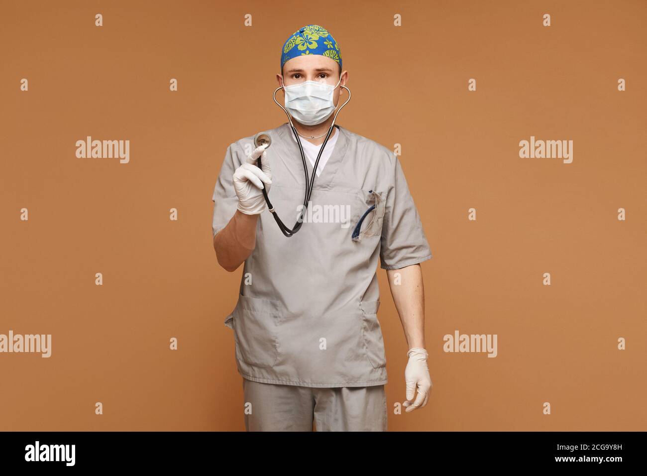 A male doctor in a medical uniform and protective face covering posing ...