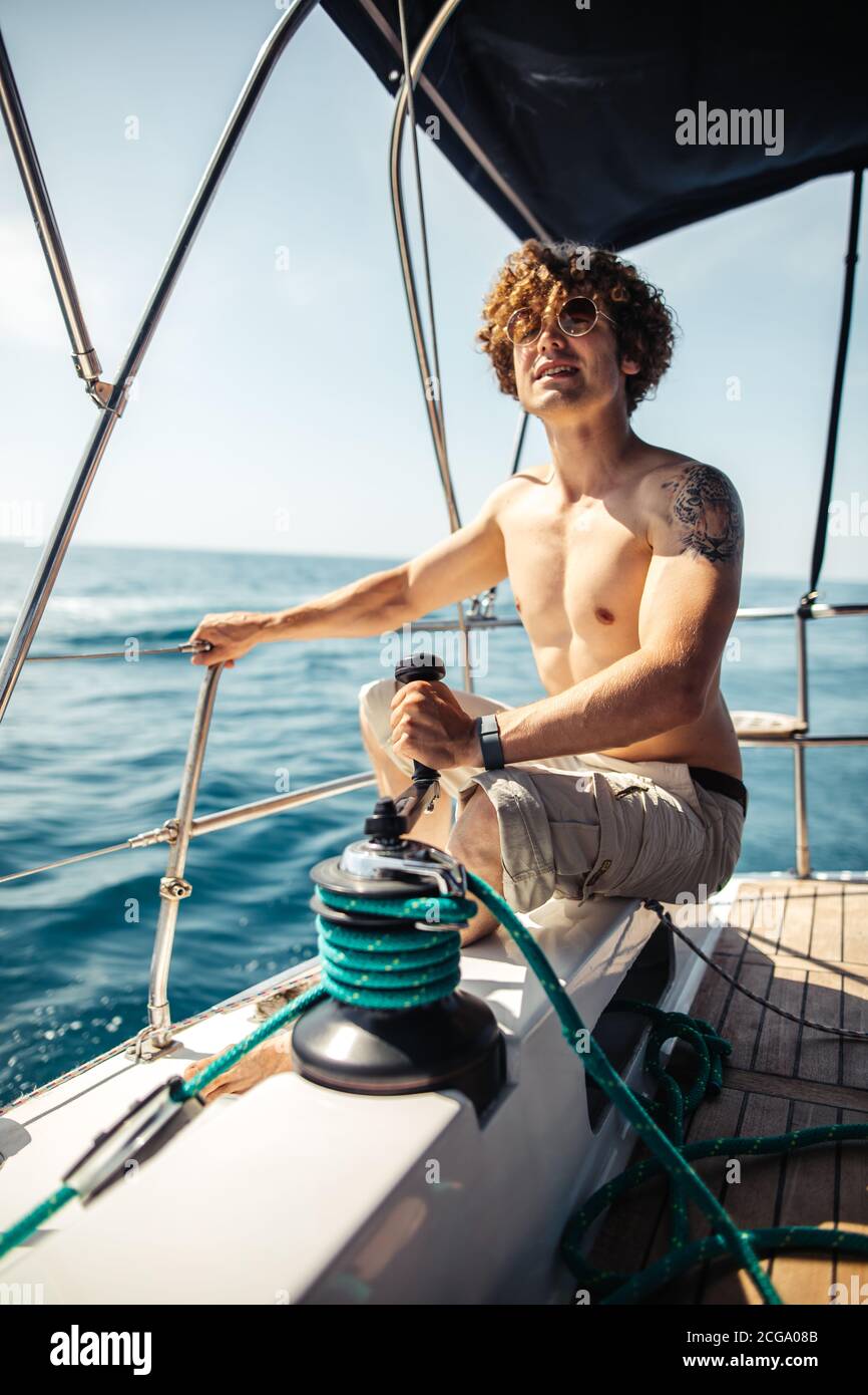 Young handsome hipster sailor man with fuzzy hairs sailing a boat to ...