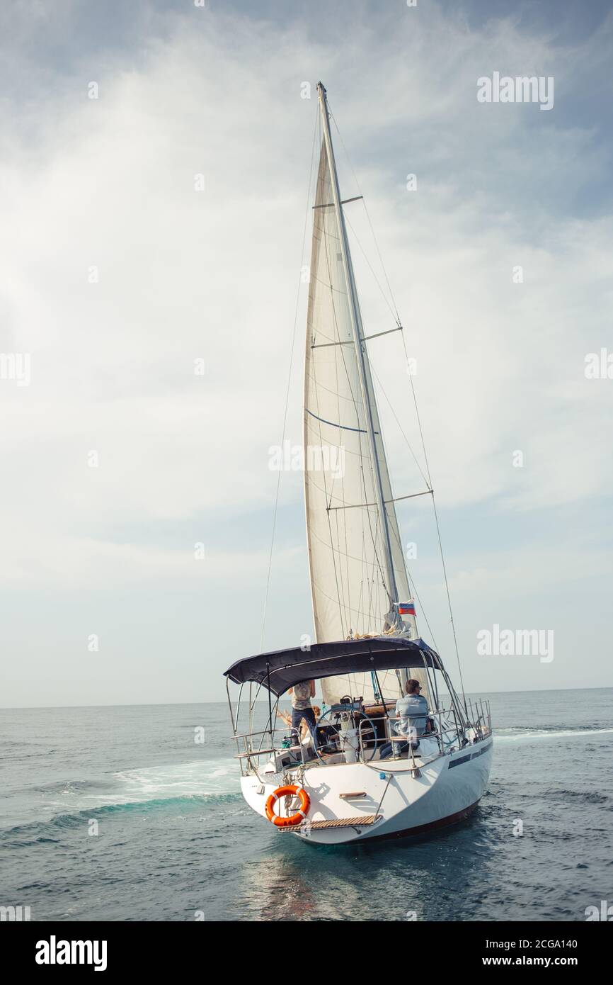 Back view of sailboat with white sails on calm sea in sunny weather ...