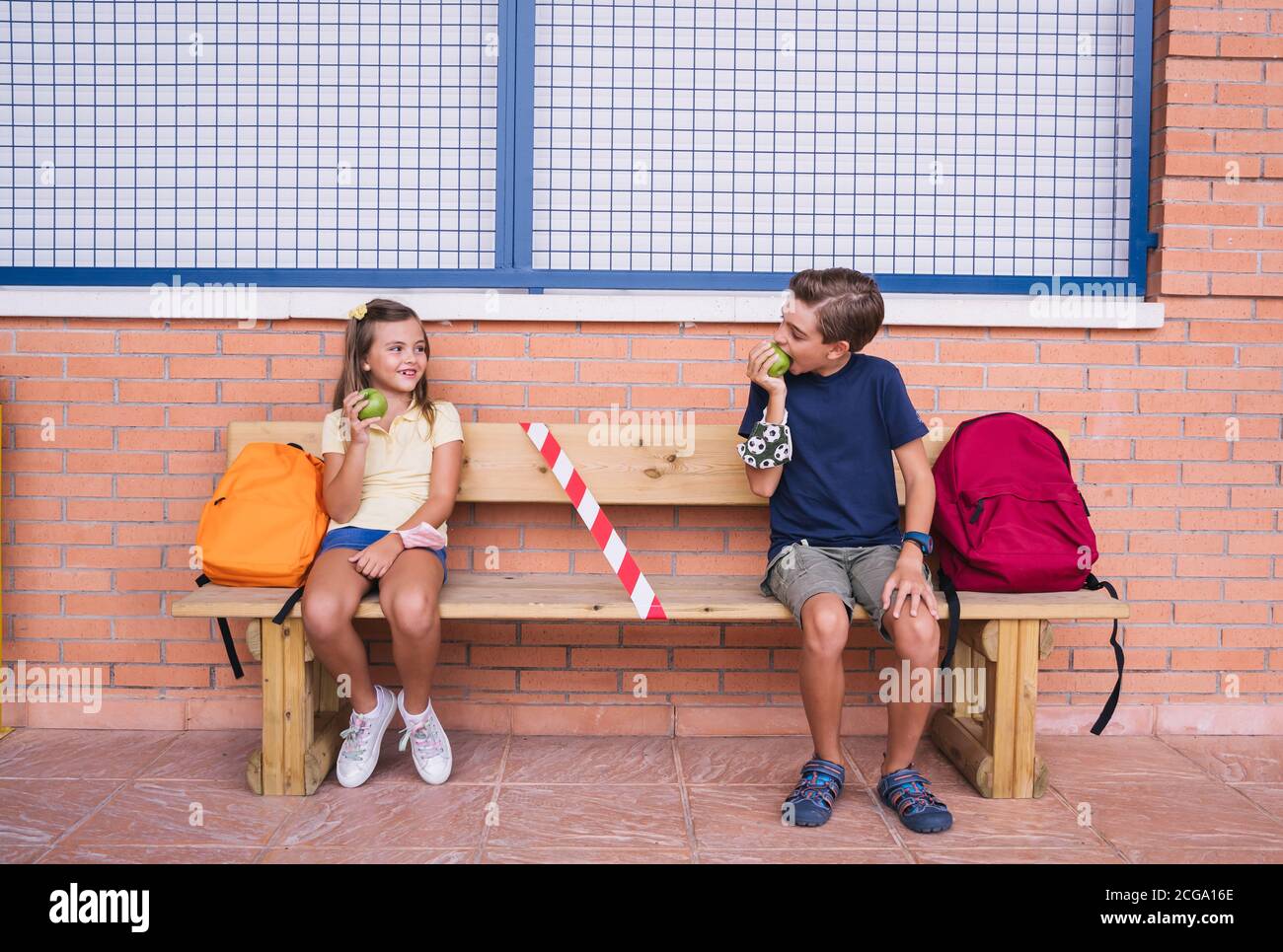 Children eating an apple at recess sitting on a bench keeping social ...