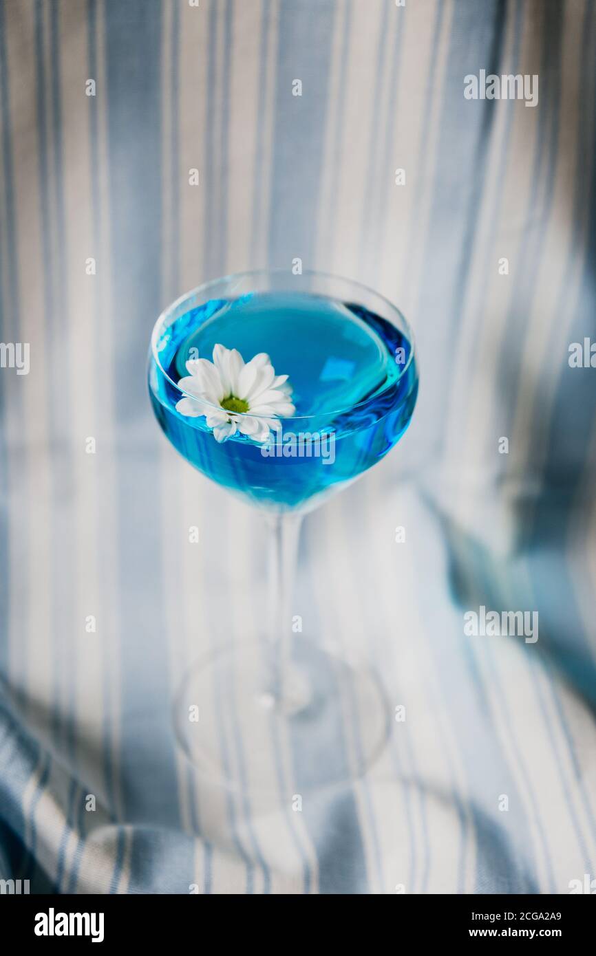 A bright blue cocktail in a nick and nora glass garnished with a ...