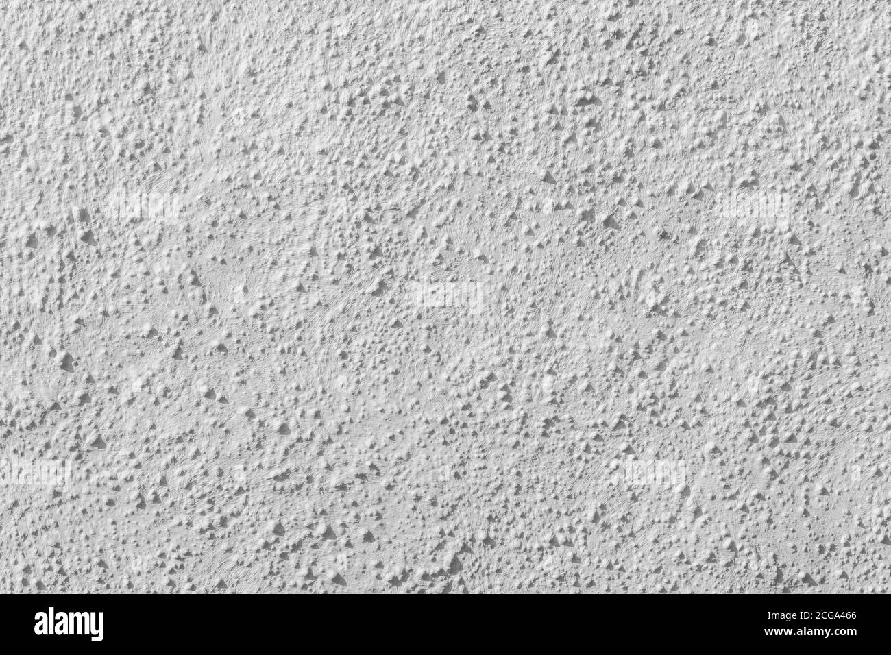 Sparsely pebble-dashed white painted wall side-lit by sunshine so it ...