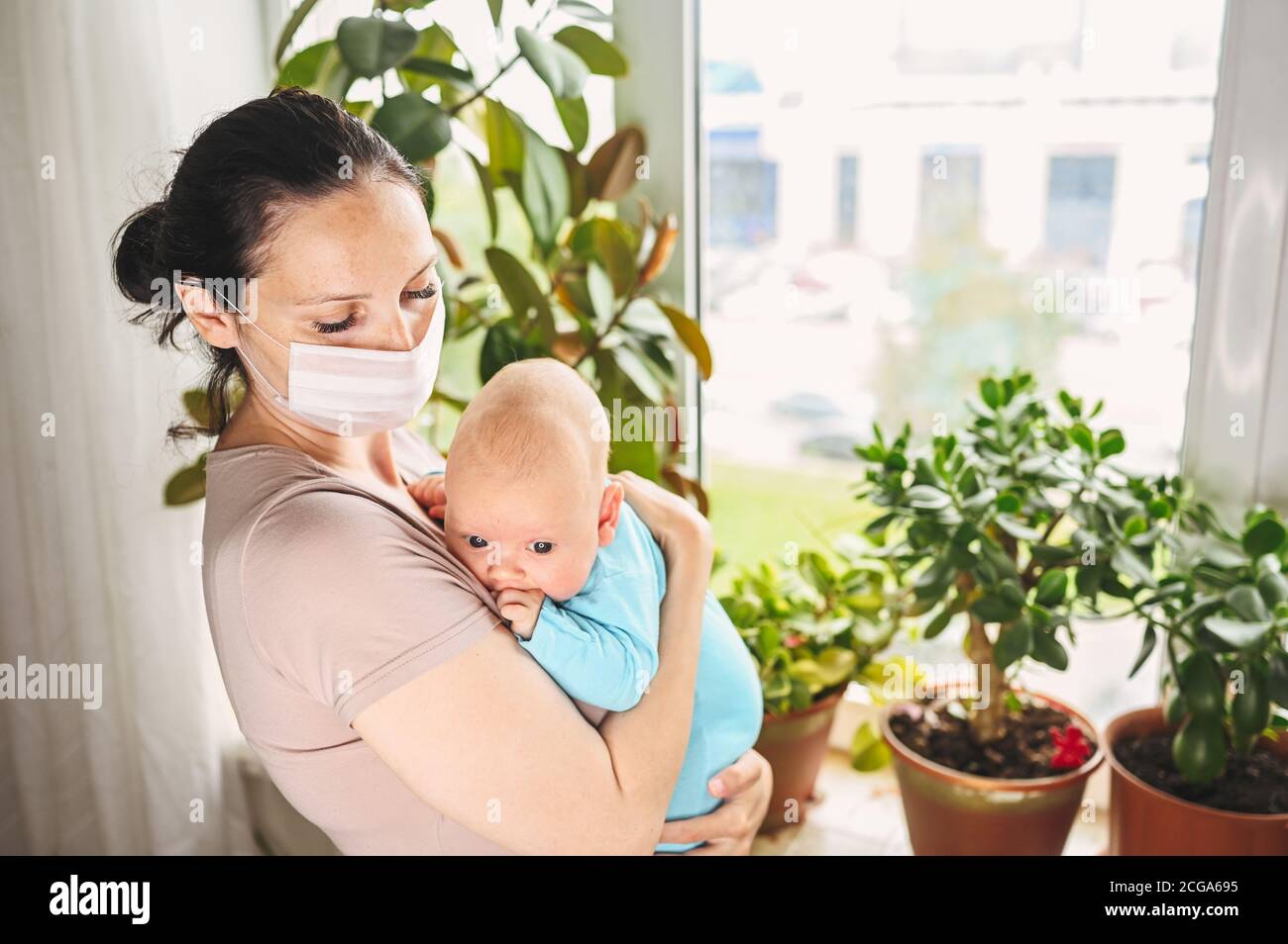 Beautiful mother in protective face mask holding her little cute ...