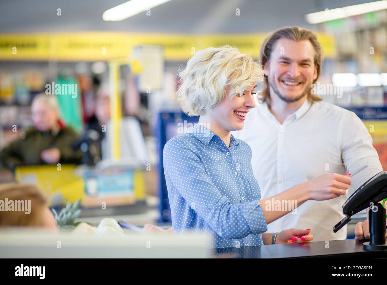 Blonde attractive woman at the supermarket checkout, she is paying ...