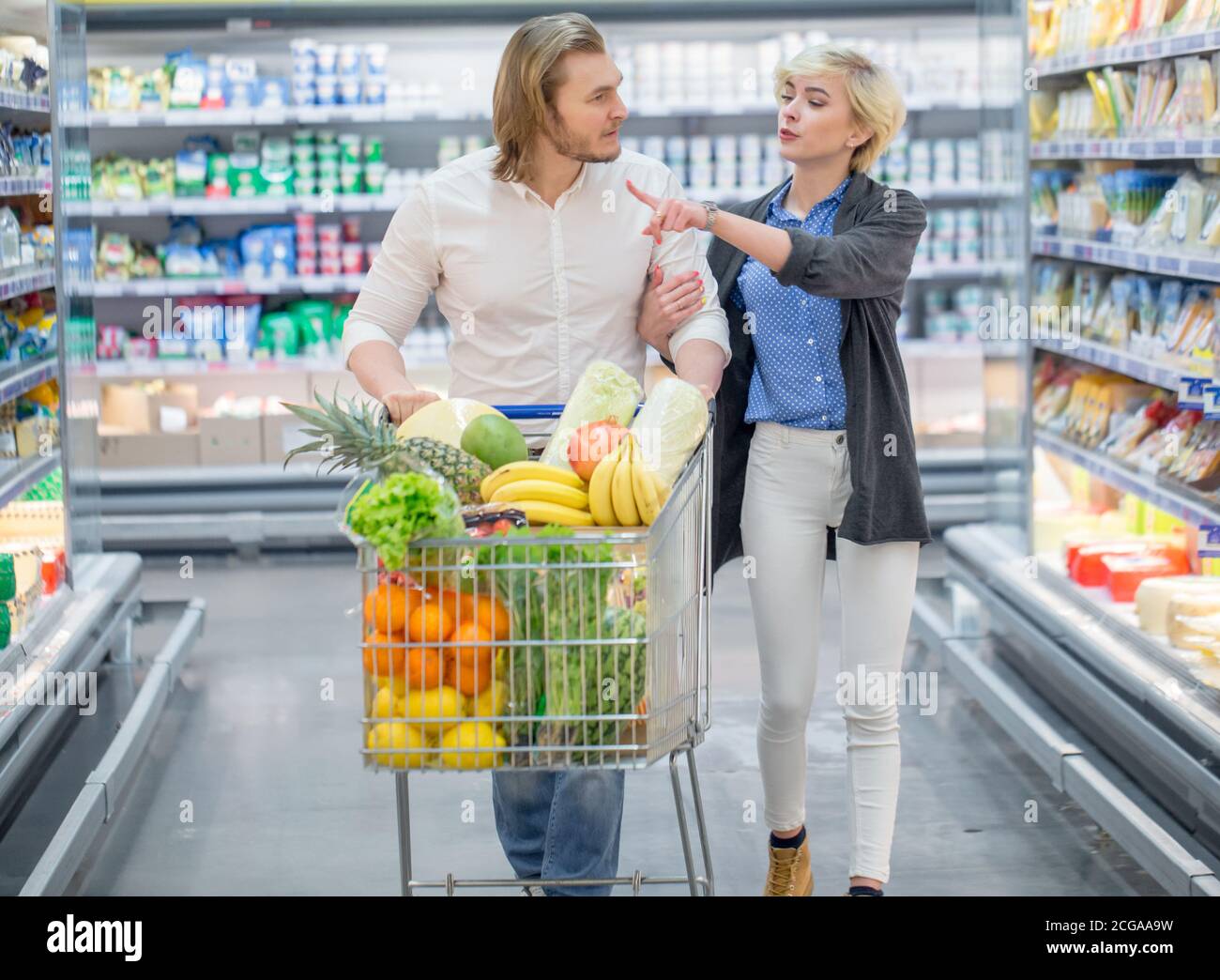 Caucasian cheerful male and female shoppers push cart with grocery ...