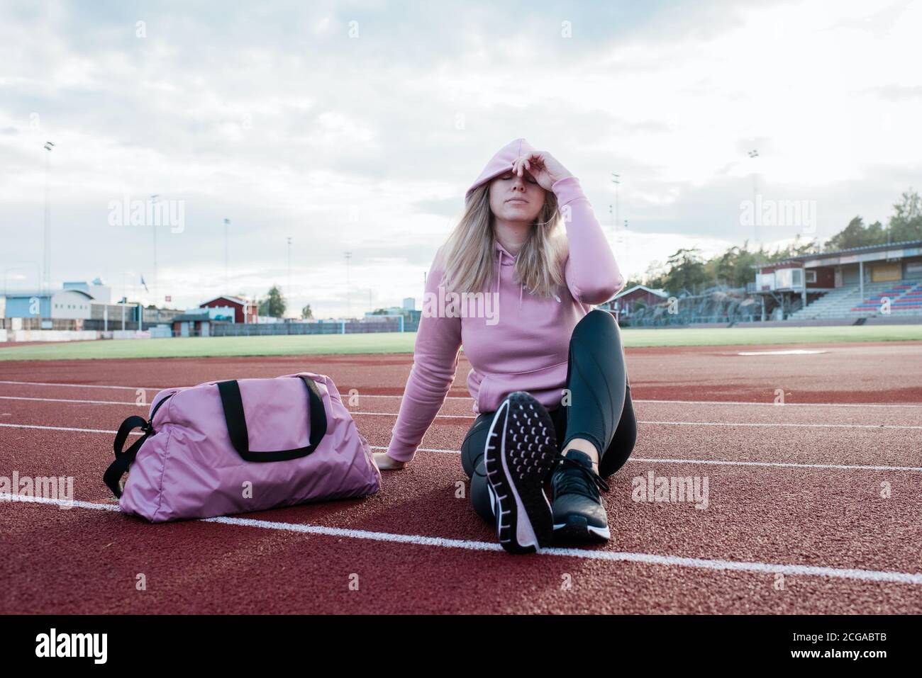 woman sat on a running track looking tired and thinking Stock Photo - Alamy