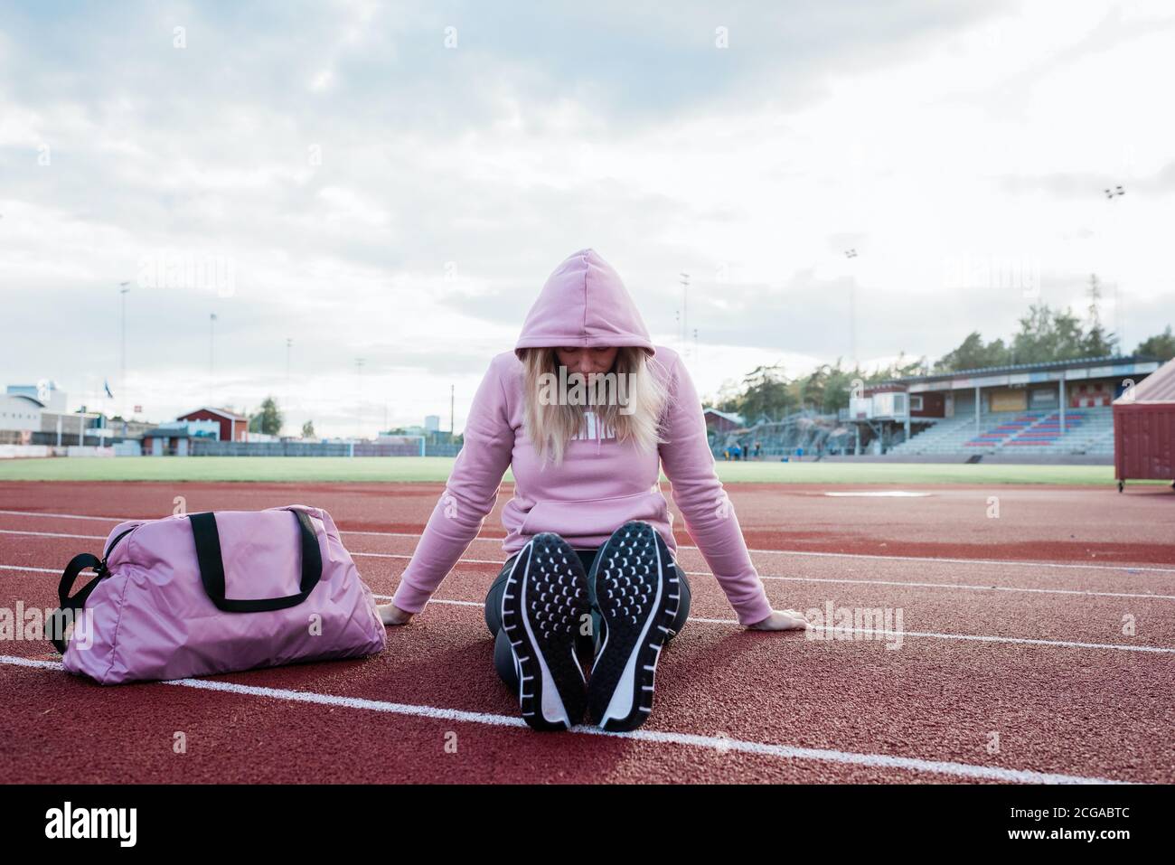 woman sat on a running track looking nervous Stock Photo - Alamy