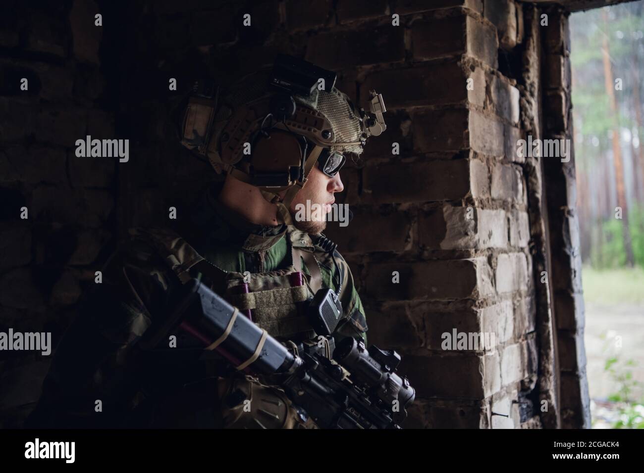 Military man with assault rifle standing inside building, he is ready ...