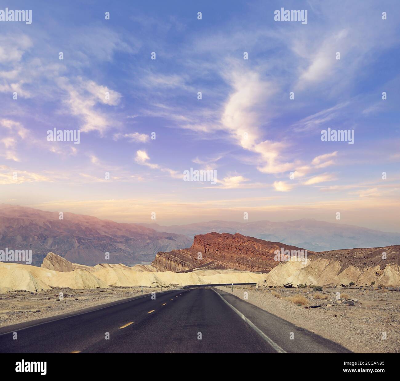 Desert road leading through Death Valley National Park at sunset ...